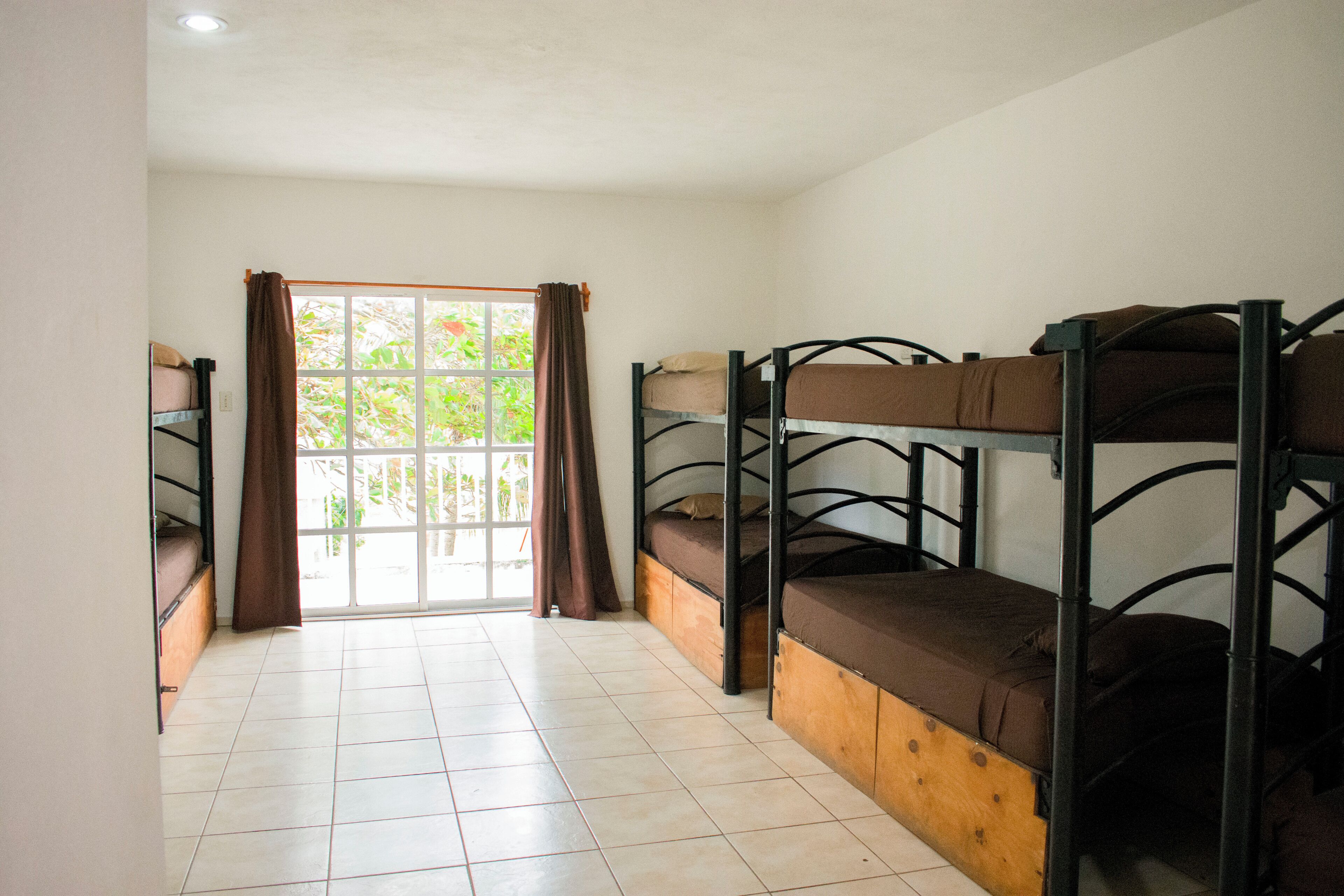 Um dormitório com beliches, uma janela com cortinas e piso de azulejos.