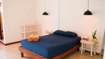 Quarto com cama de madeira, roupa de cama azul, mesa de cabeceira branca e prateleira.