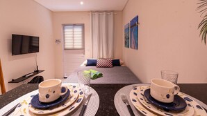 Quarto de hotel com cama, televisão, área de refeições com pratos e talheres, e janela com cortinas.