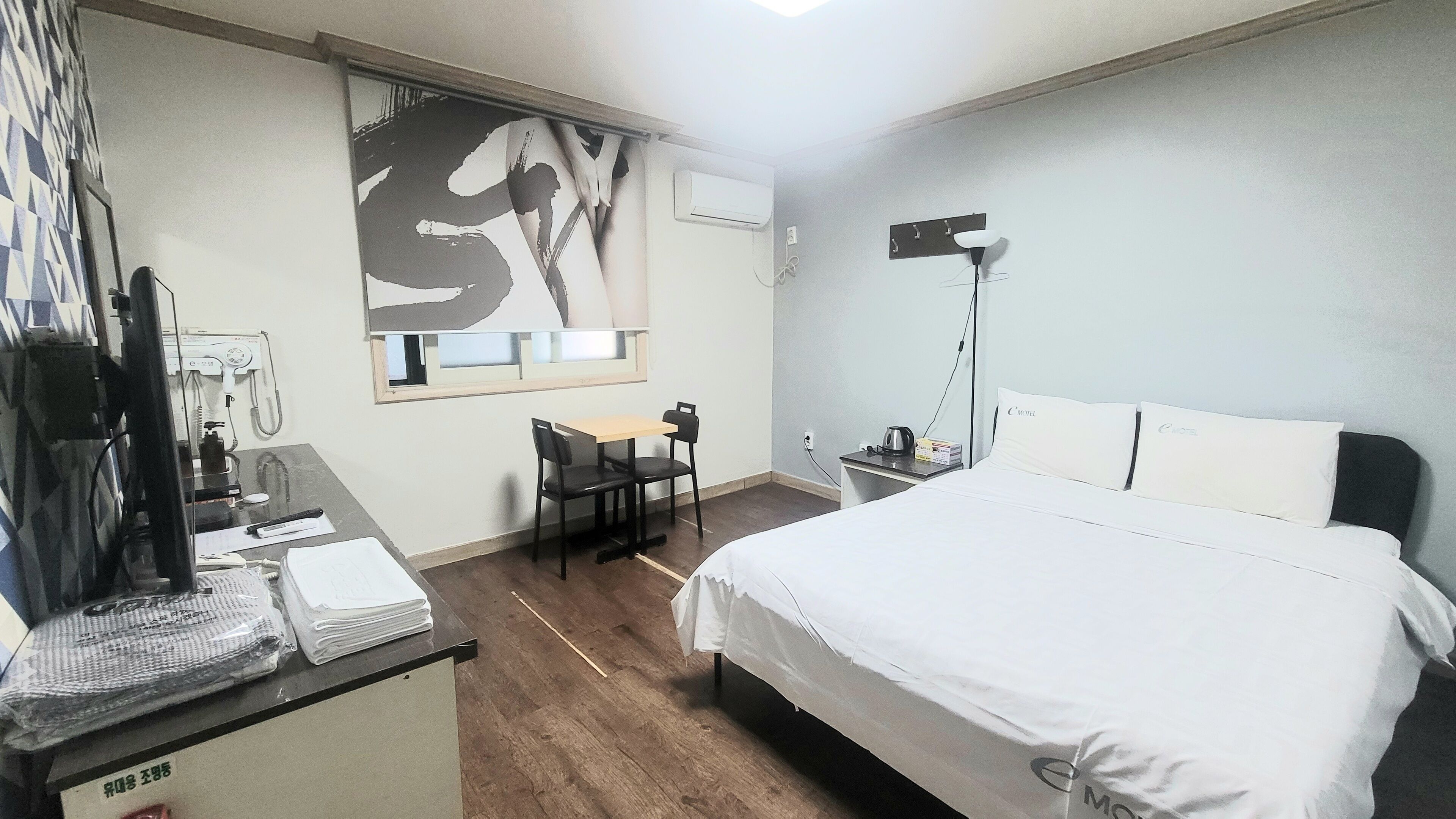 Quarto de hotel com cama, escrivaninha, cadeira e uma pintura na parede.