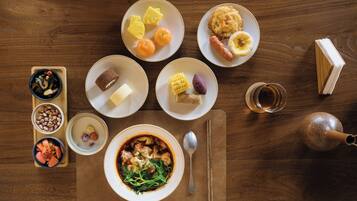 Uma mesa de madeira com diversos pratos, incluindo uma tigela de sopa, pratos com frutas e uma chaleira.