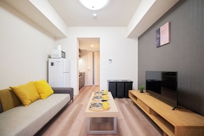 Uma sala de estar moderna com sofá, mesa de centro, televisão e uma cozinha ao fundo.