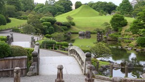 Um jardim japonês tradicional com uma ponte de pedra, um lago e uma colina.