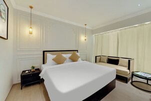 Quarto de hotel com uma cama grande, um sofá, uma mesa de cabeceira com abajur e um quadro na parede.