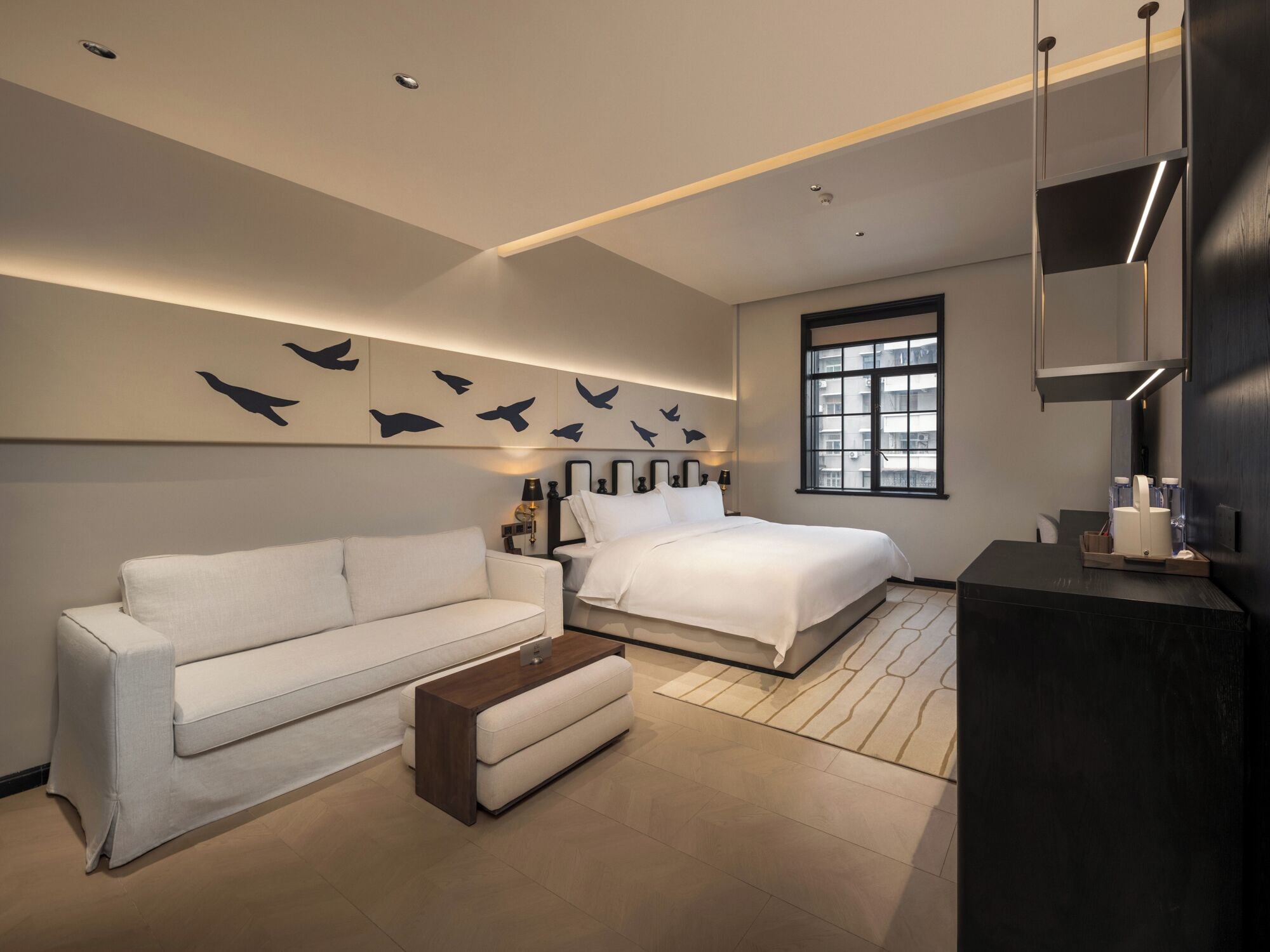 Quarto moderno com cama, sofá, mesa de centro e uma janela grande.