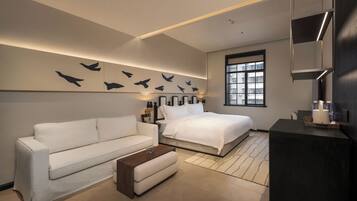 Quarto moderno com cama, sofá, mesa de centro e uma janela grande.
