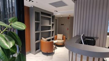 Interior moderno com balcão de recepção curvo, área de estar com duas cadeiras e uma planta grande.