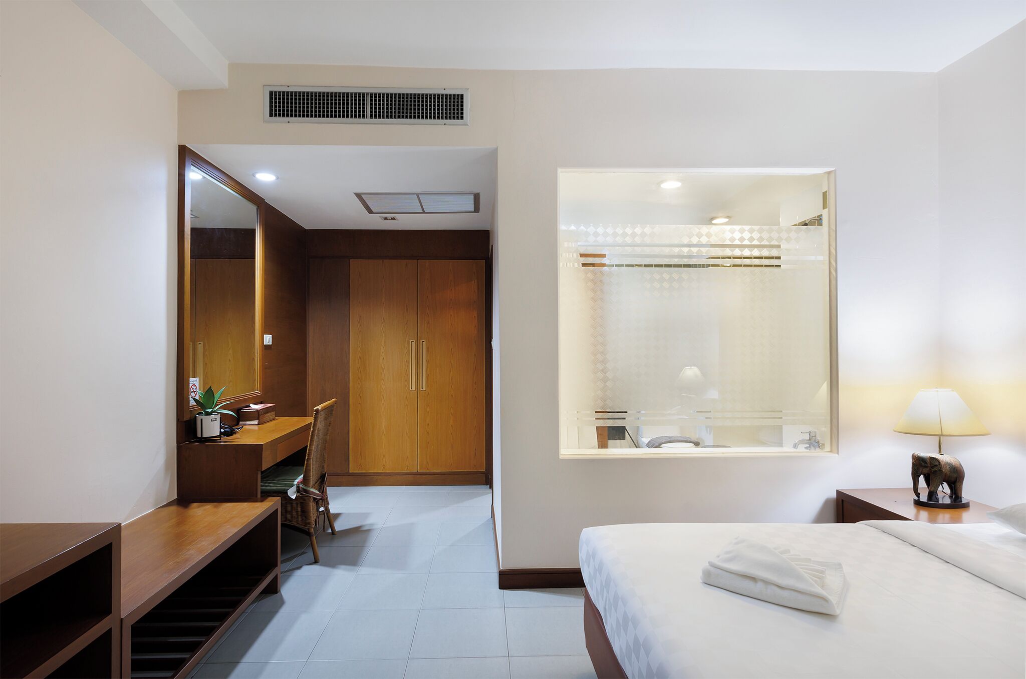 Quarto de hotel com cama, escrivaninha, cadeira, guarda-roupa e um espelho grande.