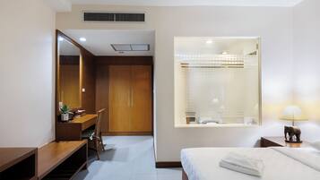 Quarto de hotel com cama, escrivaninha, cadeira, guarda-roupa e um espelho grande.