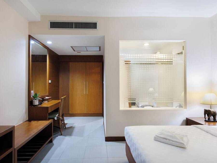 Quarto de hotel com cama, escrivaninha, cadeira, guarda-roupa e um espelho grande.