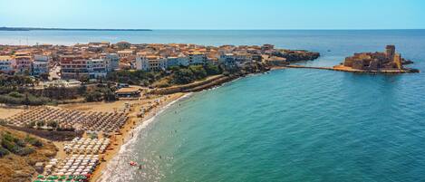 Uma vila costeira com uma praia, uma construção semelhante a um castelo e edifícios residenciais.