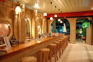 Uma área de bar com balcão extenso, vários bancos e luminárias pendentes.