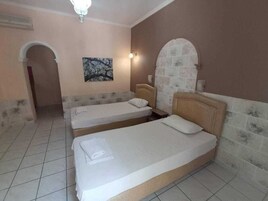 Quarto de hotel com duas camas de solteiro, piso de azulejos, um quadro na parede e um arco de pedra.