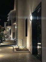 Um edifício moderno com design limpo e minimalista, apresentando um caminho central, uma pequena área ajardinada e uma porta de entrada ampla.