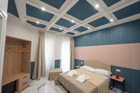 Um quarto com cama, guarda-roupa de madeira, uma mesinha e um criado-mudo.