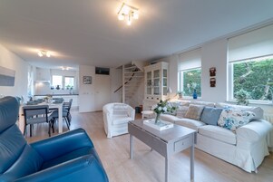 Uma sala de estar moderna com área de jantar, mobiliário branco, escada e janelas amplas.