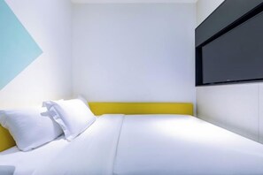 Quarto de hotel moderno com cama, roupa de cama branca, cabeceira amarela e televisão de tela plana fixada na parede.