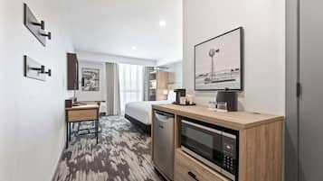 Quarto de hotel moderno com uma cama, uma escrivaninha, micro-ondas, máquina de café e uma janela grande com cortinas.