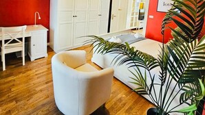 Um espaço compacto com cozinha americana, um sofá branco, uma mesinha pequena e um vaso de planta.