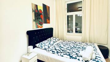 Quarto com teto de madeira, cama com roupa de cama estampada, mesa de cabeceira e janela com cortinas.