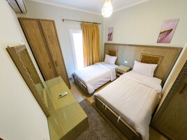 Quarto de hotel com duas camas, uma mesa de cabeceira com controle remoto, um espelho e uma janela com cortinas.