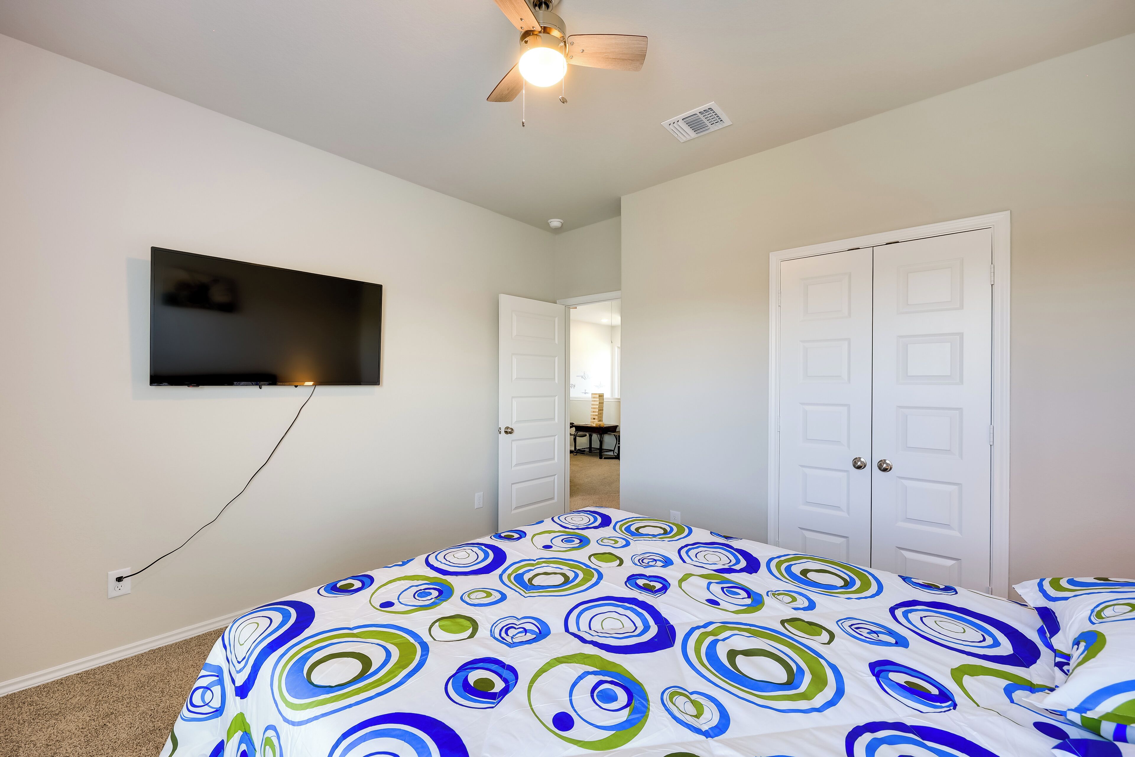 Quarto com cama, ventilador de teto, televisão fixada na parede e porta que dá para outro cômodo.