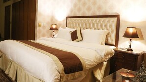Cama bem arrumada com detalhe em castanho, duas mesas de cabeceira com abajures e parede estampada.