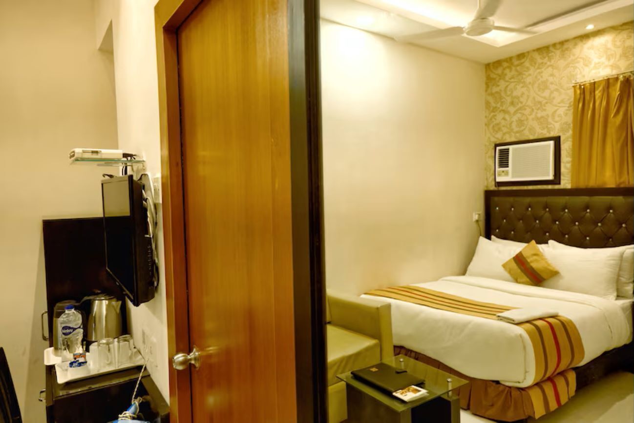 Quarto de hotel com cama, mesa de cabeceira e televisão fixada na parede.