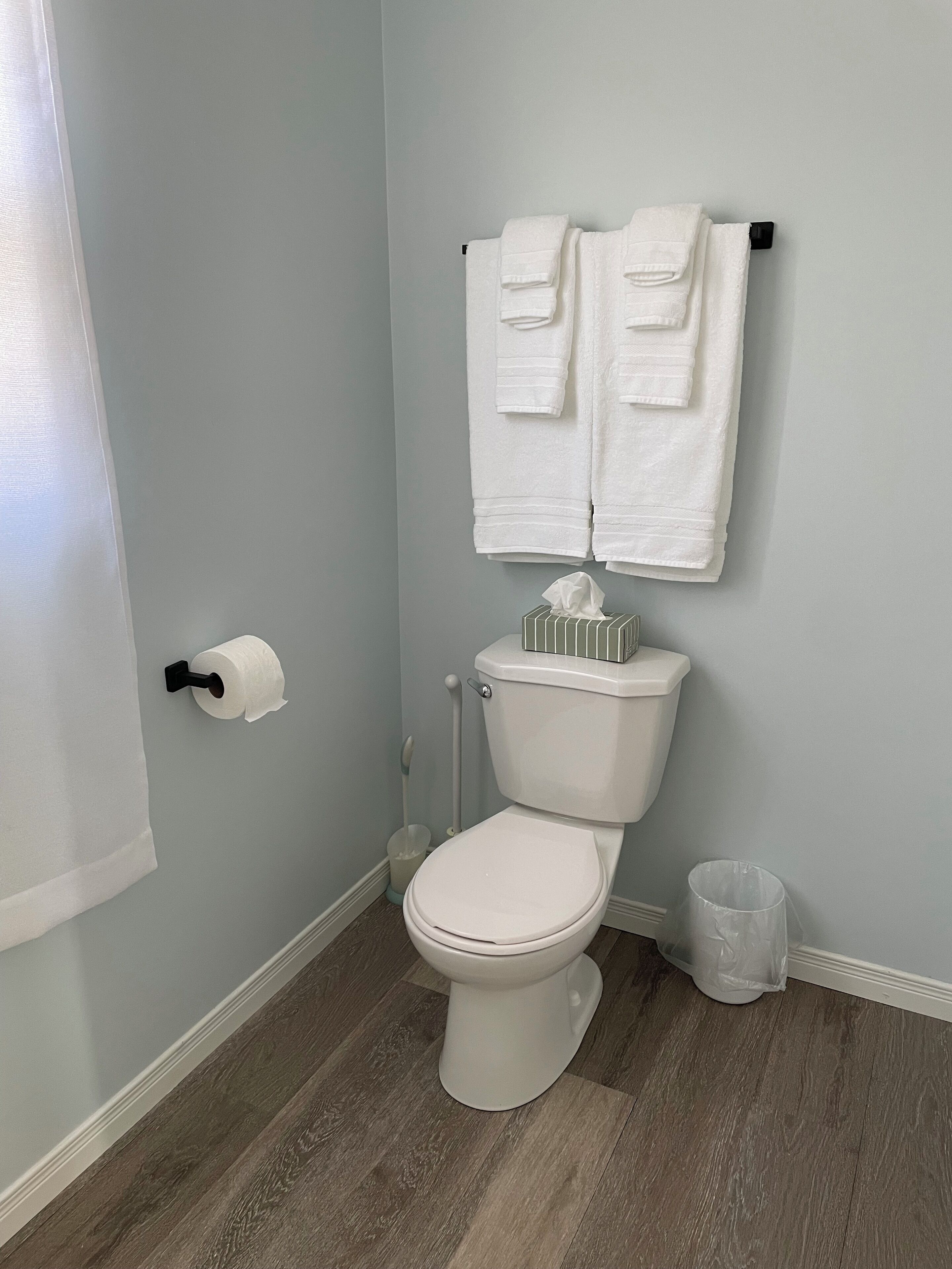 Um banheiro com vaso sanitário, porta-toalhas com duas toalhas, rolo de papel higiênico e lixeira.
