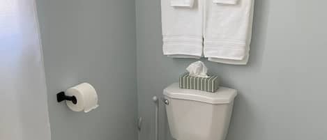 Um banheiro com vaso sanitário, porta-toalhas com duas toalhas, rolo de papel higiênico e lixeira.