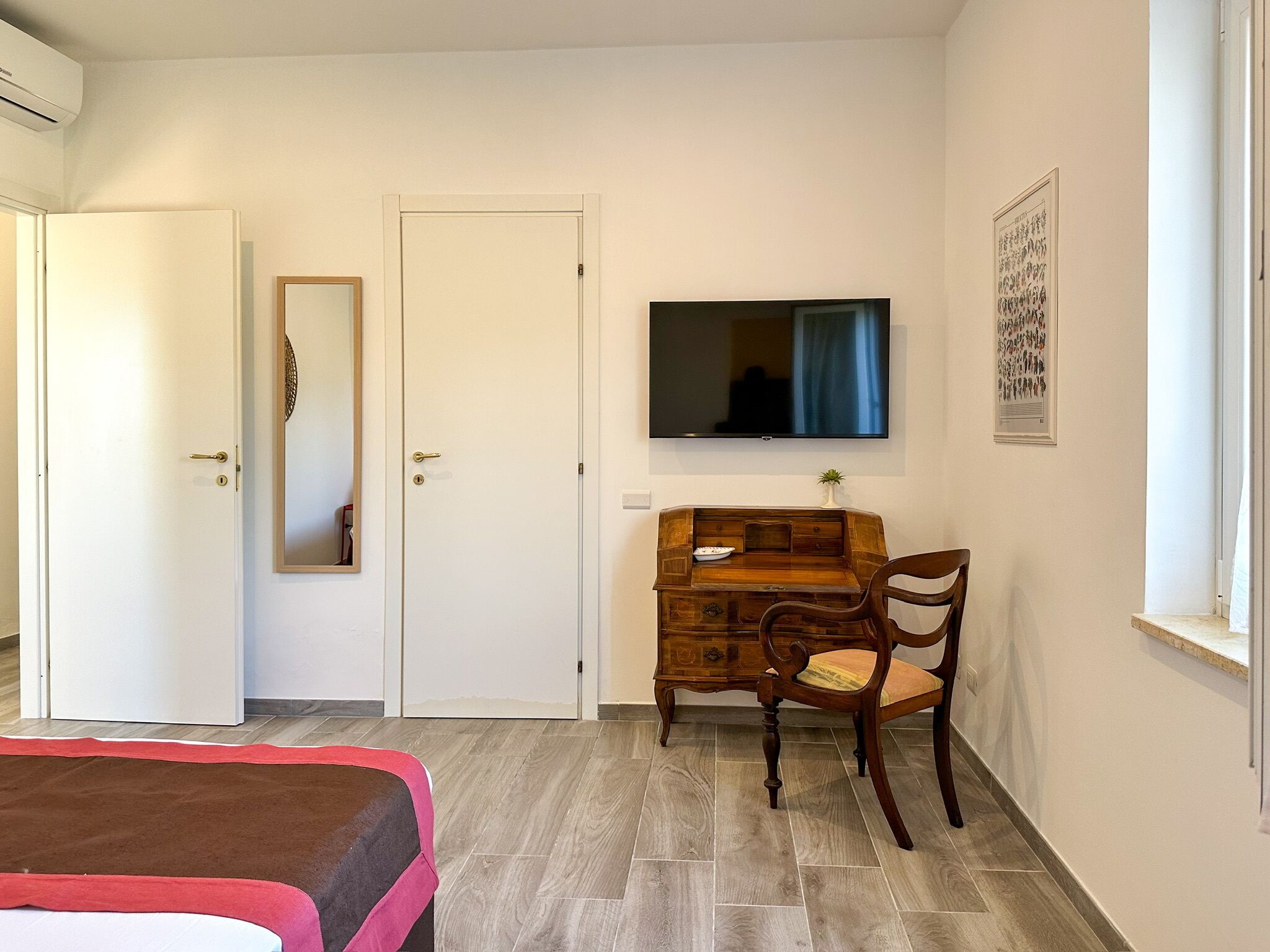 Quarto com cama, cómoda de madeira, cadeira, televisão e espelho.