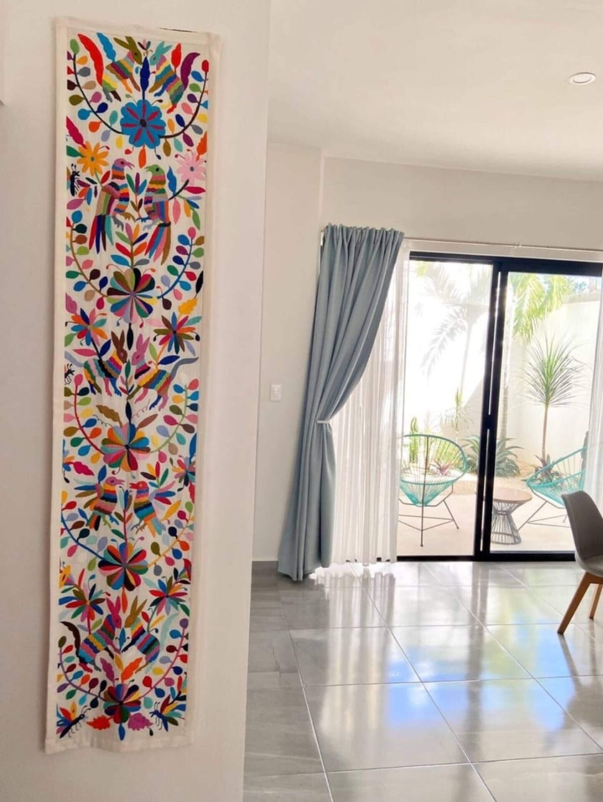 Quarto com um grande tapeçaria floral, porta de correr de vidro que dá para área externa com cadeiras e plantas.