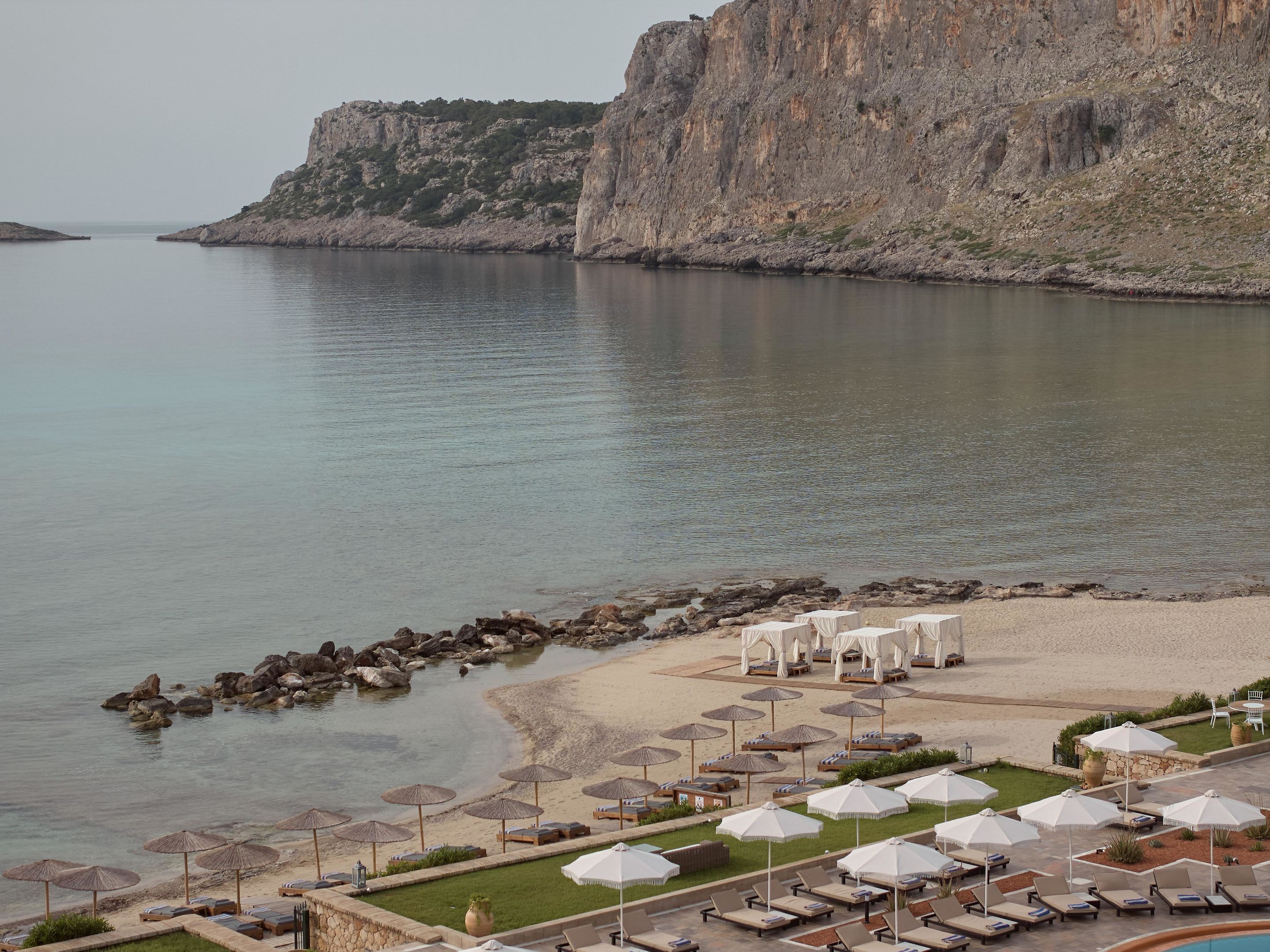 Um resort à beira-mar com espreguiçadeiras, guarda-sóis e um penhasco rochoso ao fundo.