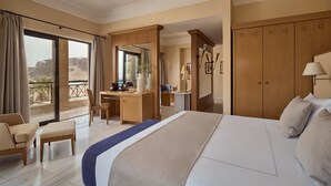 Quarto de hotel com uma cama grande, uma escrivaninha, uma cadeira e uma varanda com vista para as montanhas.