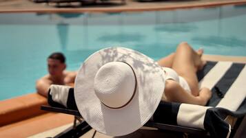 Uma área à beira da piscina com espreguiçadeiras e uma pessoa relaxando em uma delas.