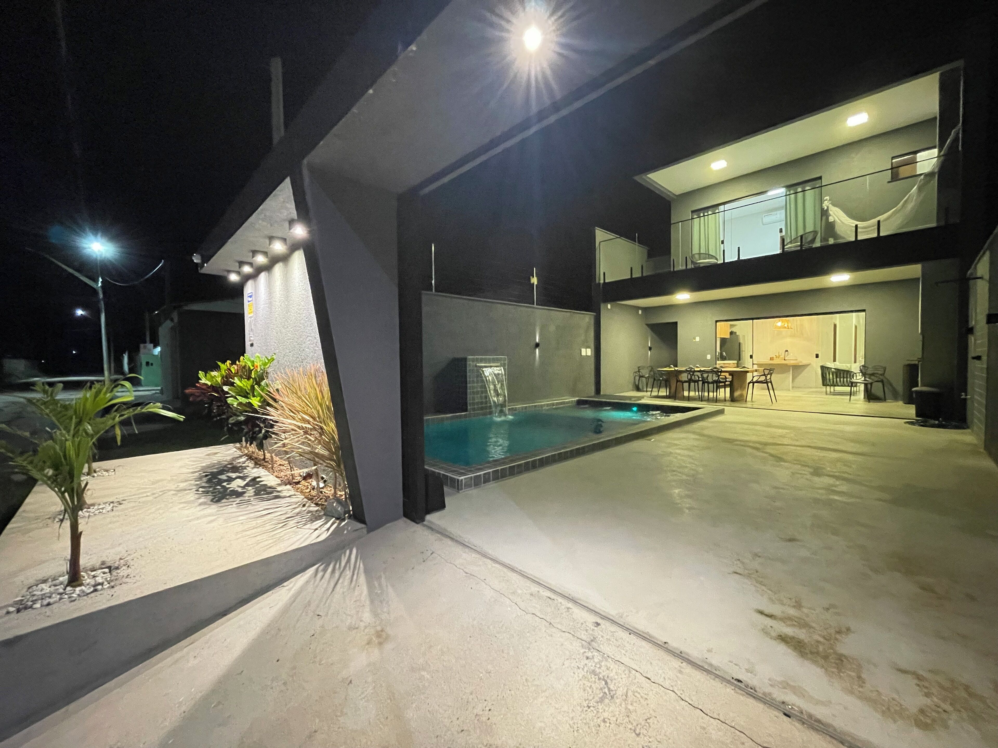 Uma casa moderna de dois andares com piscina, área de estar externa e um alpendre bem iluminado.