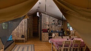 Um interior acolhedor com uma mesa de jantar de madeira posta para quatro pessoas, uma área de cozinha com micro-ondas vermelho e um banco de madeira rústico.