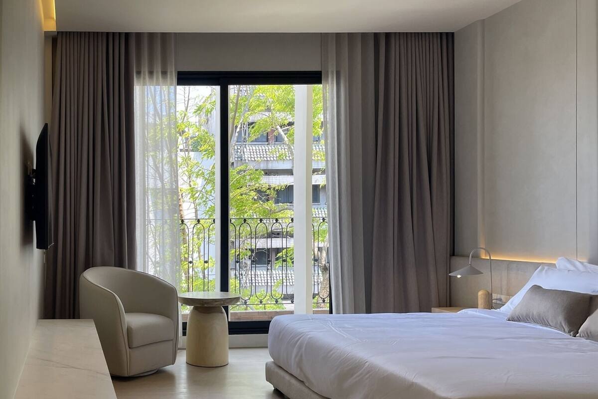 Quarto de hotel moderno com uma cama grande, um sofá, uma mesa pequena e uma TV fixada na parede.