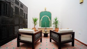Um pátio com duas cadeiras de madeira, uma mesa pequena e plantas em vasos.