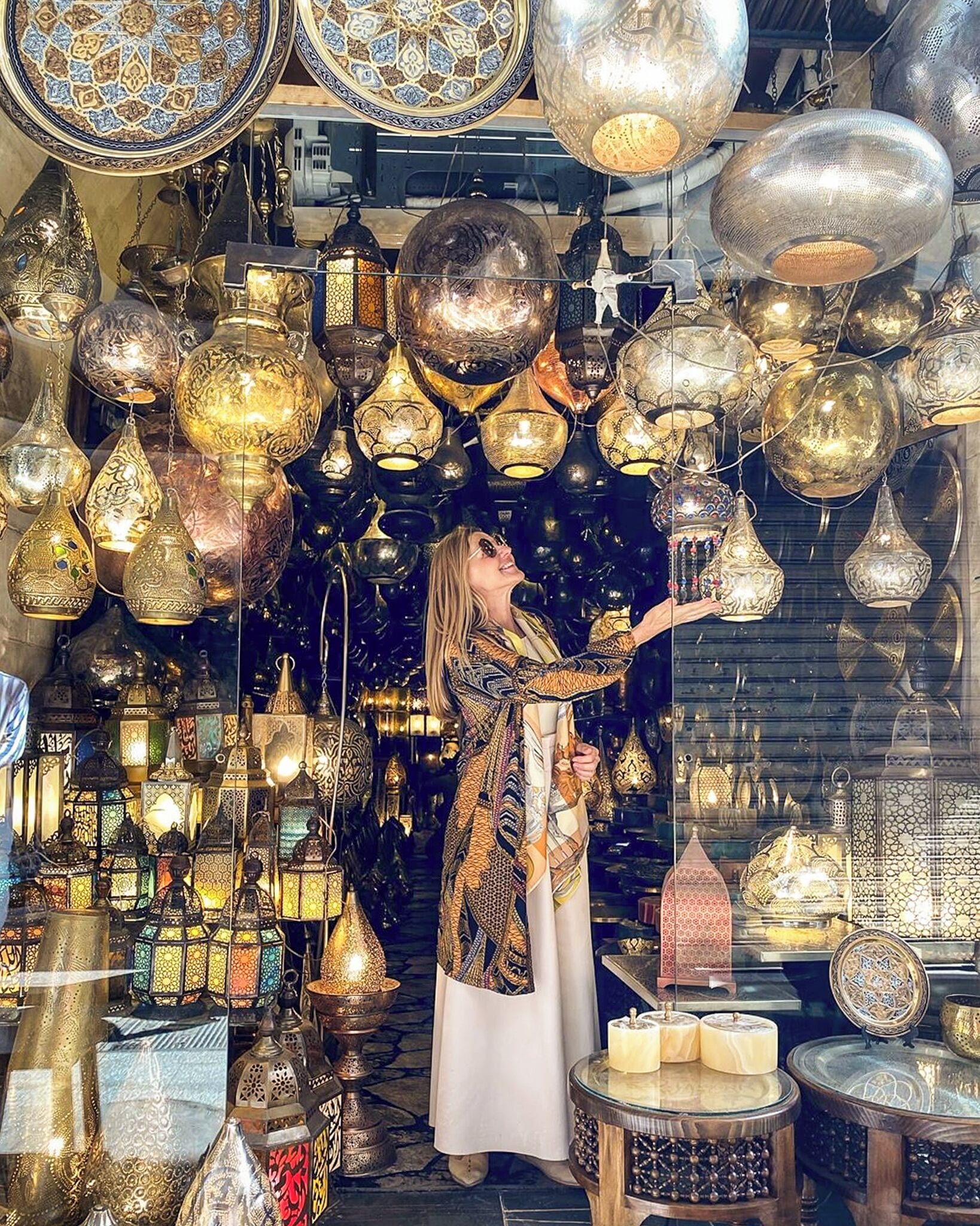 Uma mulher observa vários candelabros elaborados em uma loja bem iluminada.