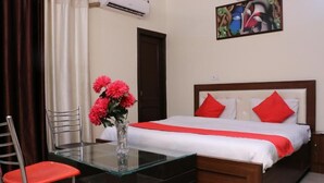 Quarto de hotel com cama, mesa de vidro, cadeira e um vaso de flores.