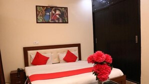 Quarto de hotel com cama, mesa de cabeceira, um vaso com flores e um quadro na parede.