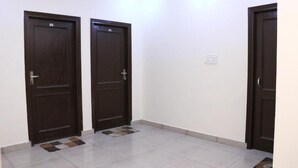 Um corredor com três portas de madeira escura, paredes brancas e chão de azulejos.