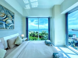 Quarto moderno com uma cama grande, vista para o mar e para a cidade.