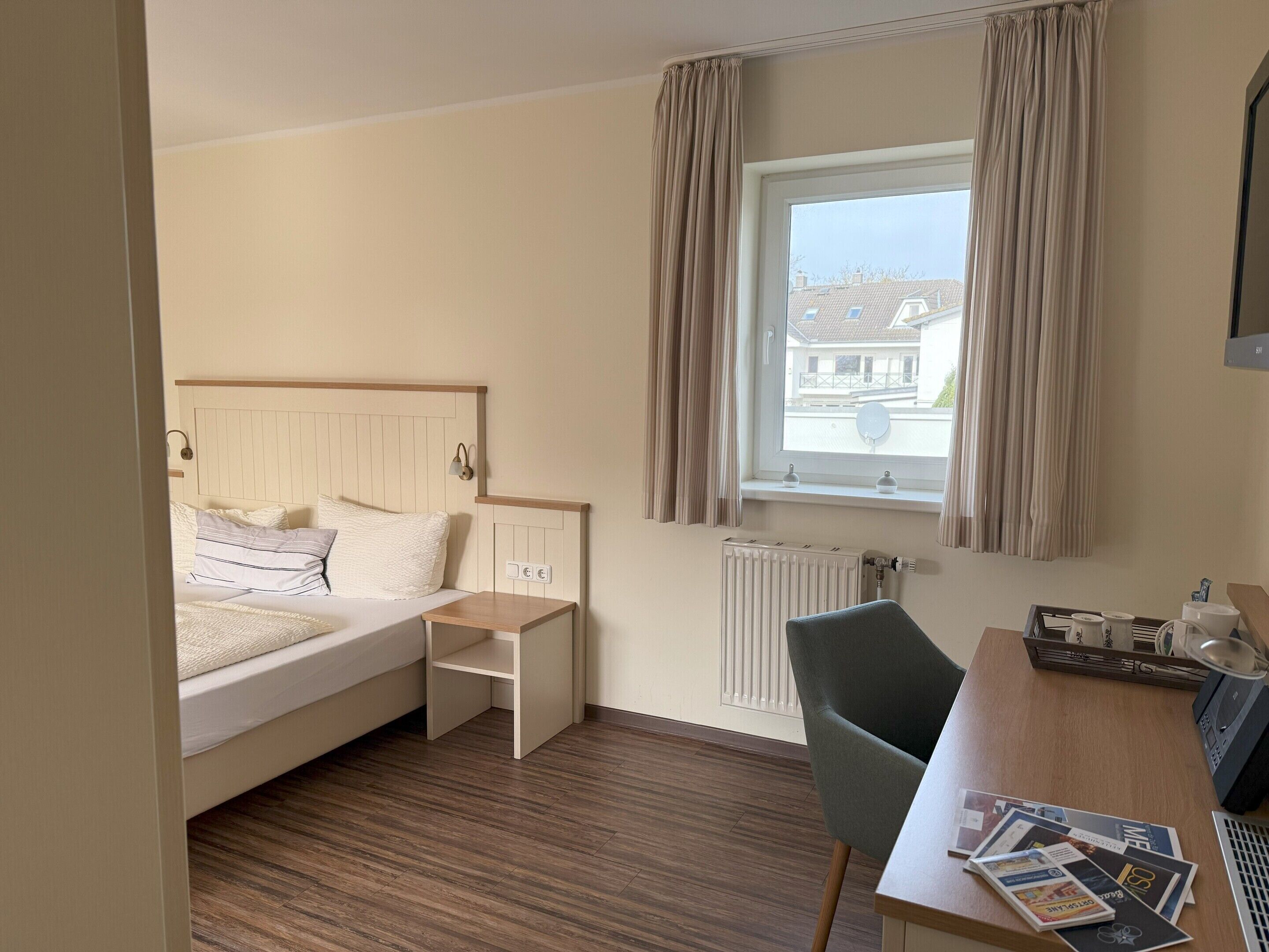 Quarto de hotel com cama, mesa de cabeceira, cadeira e janela com cortinas.