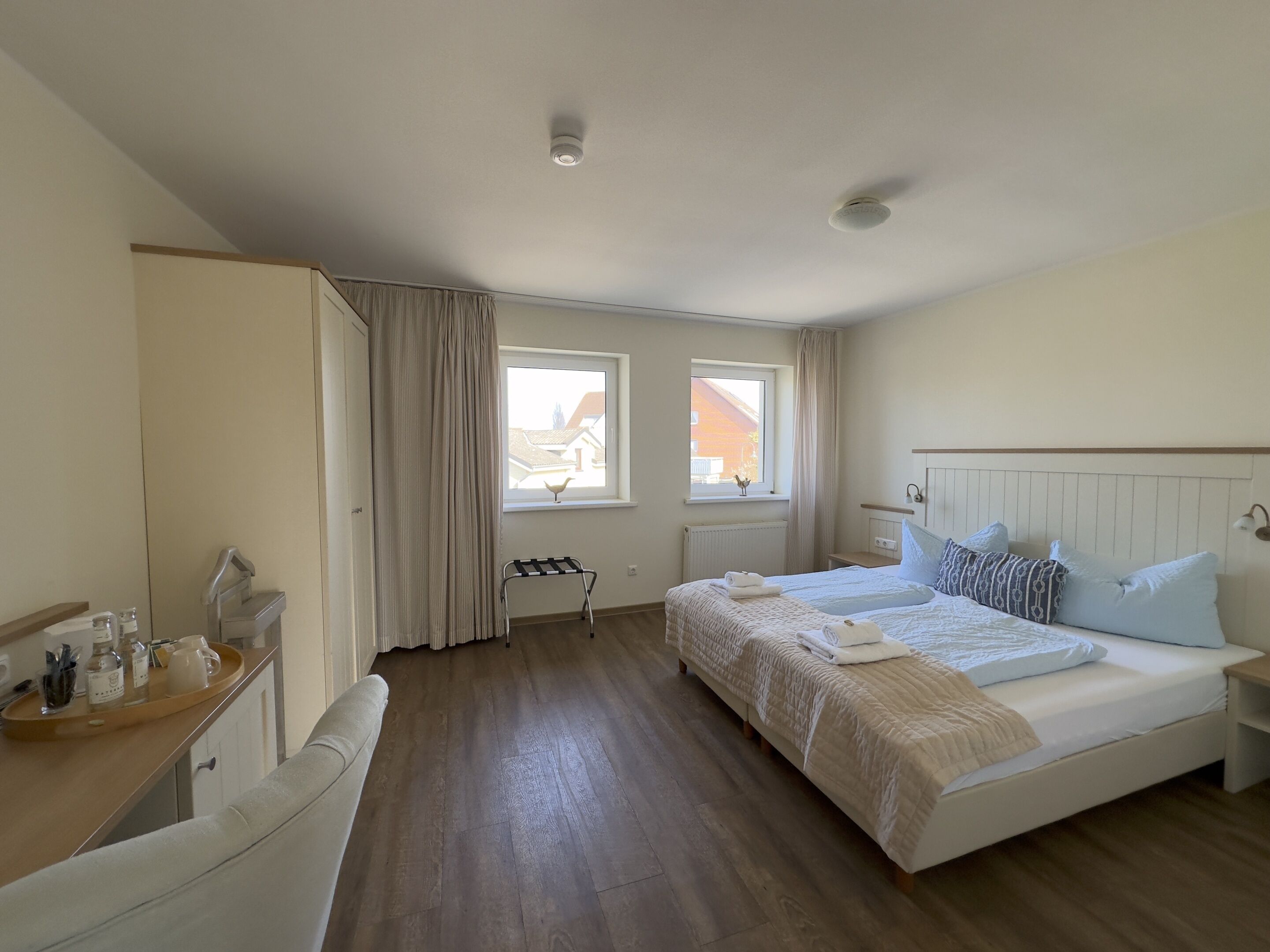 Quarto com cama, mesas de cabeceira, janela, radiador e porta-toalhas.