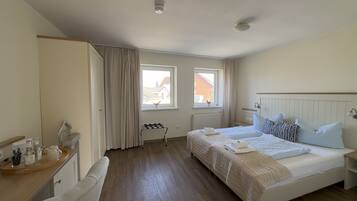 Quarto com cama, mesas de cabeceira, janela, radiador e porta-toalhas.