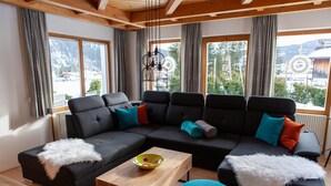 Uma sala de estar moderna com um sofá seccional, uma mesa de centro de madeira e vista para uma paisagem nevada através de grandes janelas.