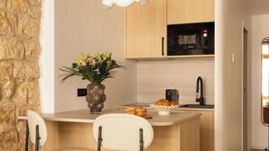 Uma cozinha moderna com ilha central, banquetas, parede de pedra, armários de madeira e luminária pendente.