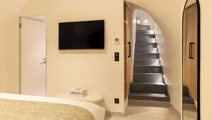 Quarto com cama, televisão fixada na parede, escada e porta.